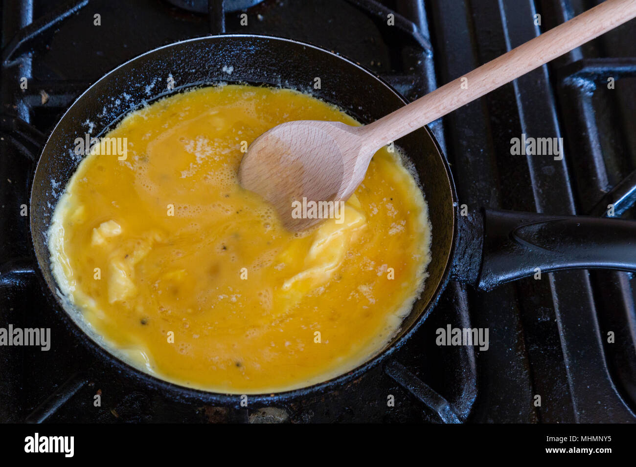 Scrambled eggs cooking in pan with wooden spoon Stock Photo - Alamy