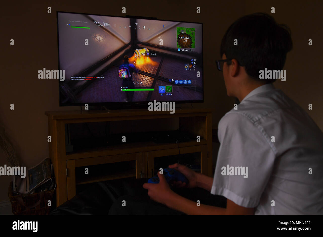A teenager boy plays the hit computer game Fortnite on a large TV on a ...