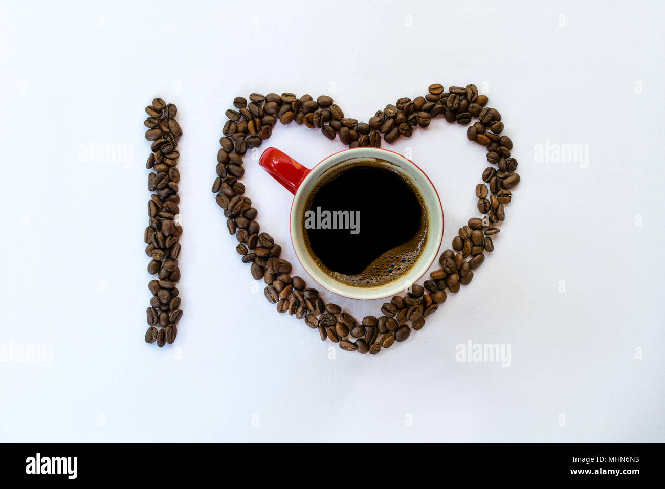 Red coffee cup placed inside coffee beans in heart shape, top view. I ...