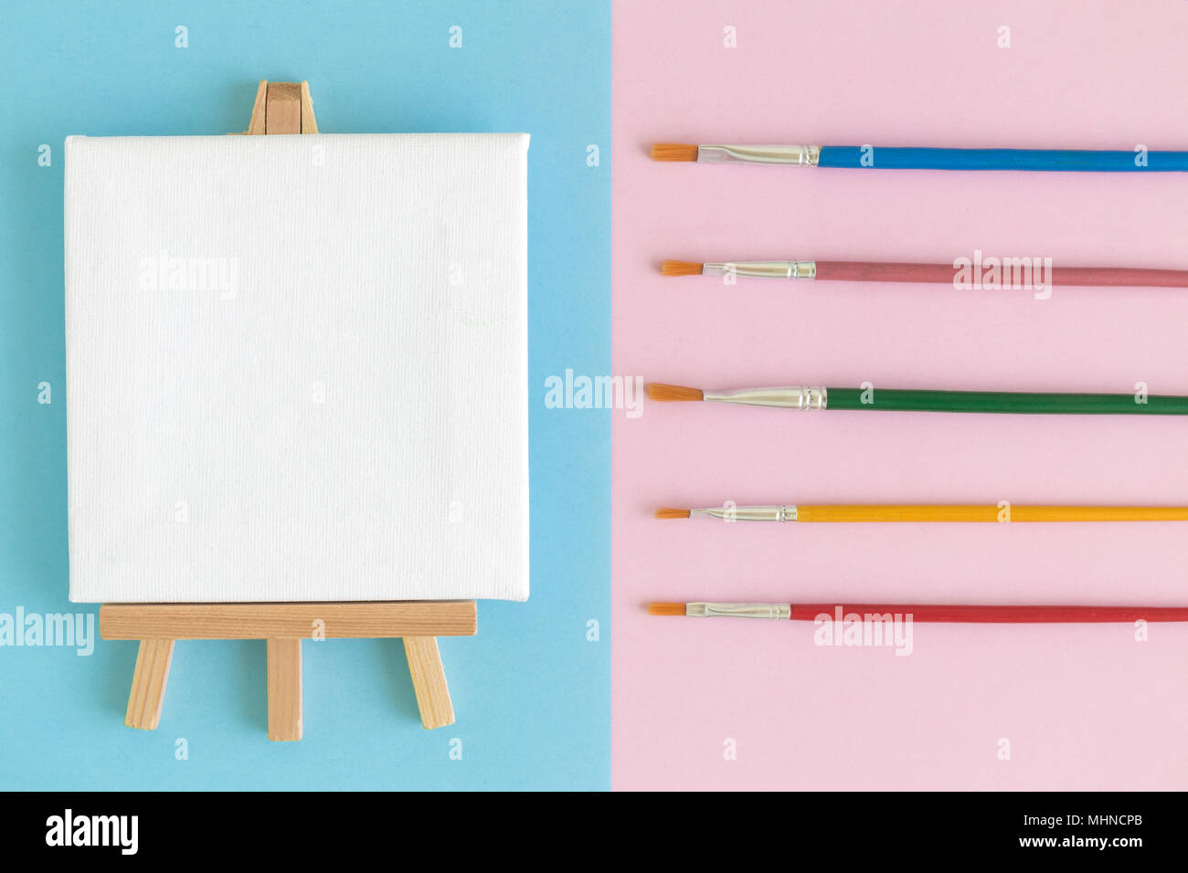 Flat lay of art canvas on easel and colorful paintbrushes on blue and ...