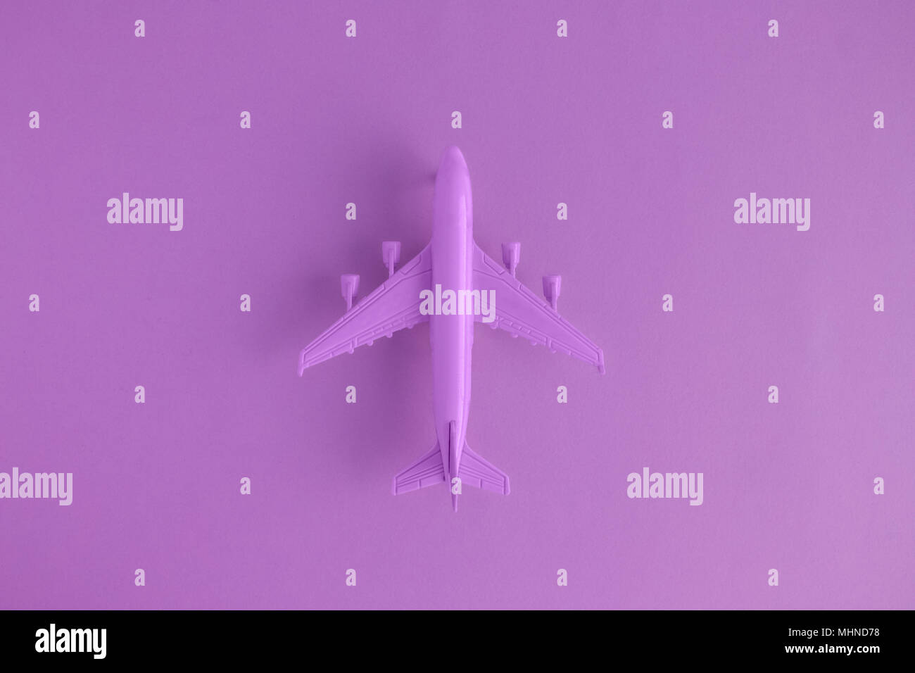 Flat lay of miniature toy airplane on violet background minimal trip ...