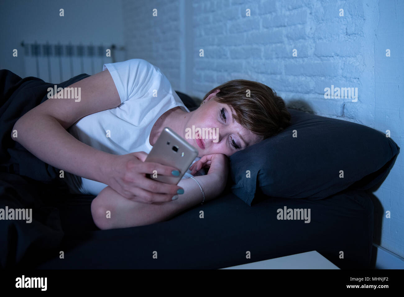 Young attractive woman awake late at night using smart phone lying ...