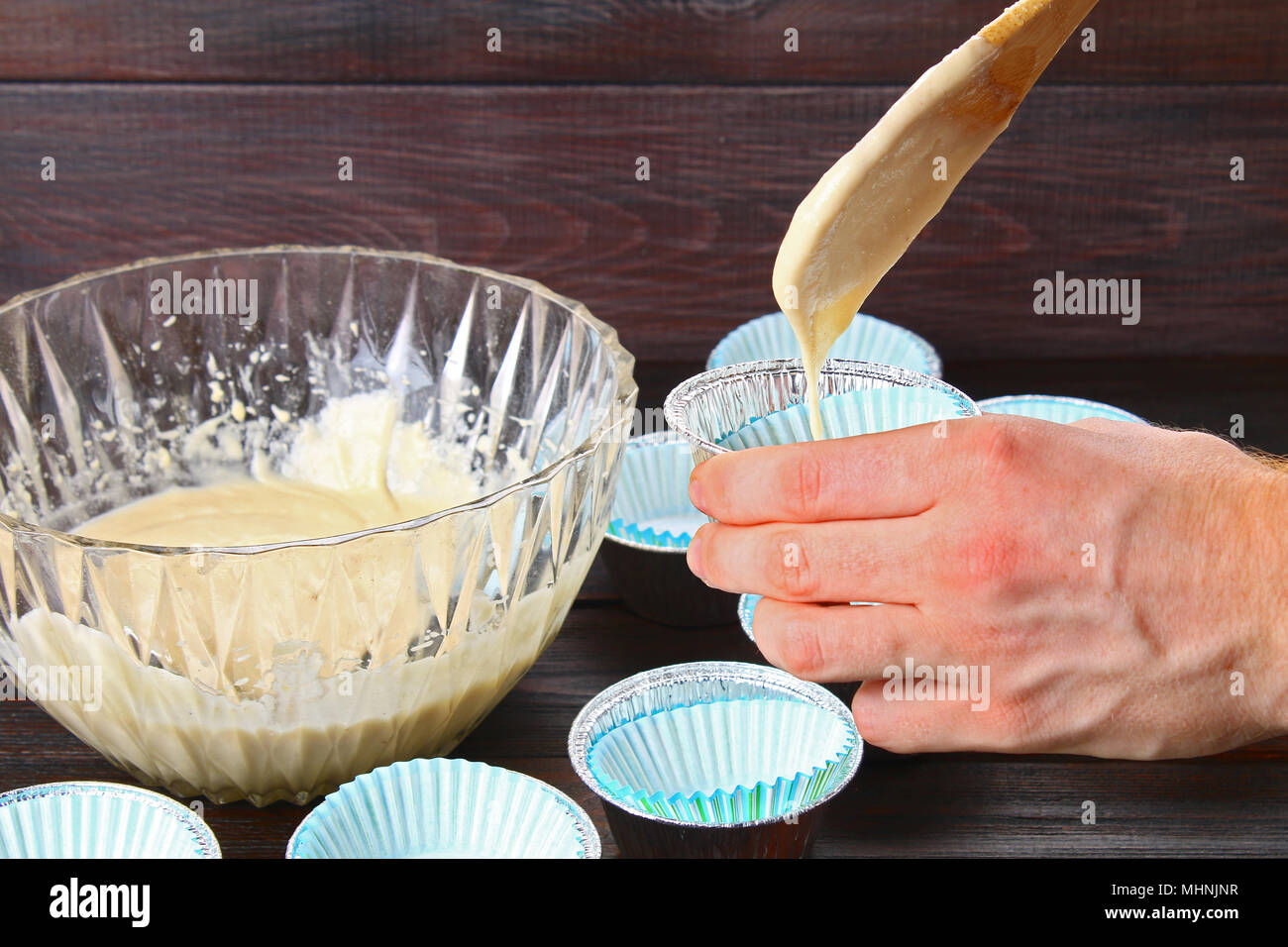 Hands pouring dough into molds for muffins on a wooden table Stock ...