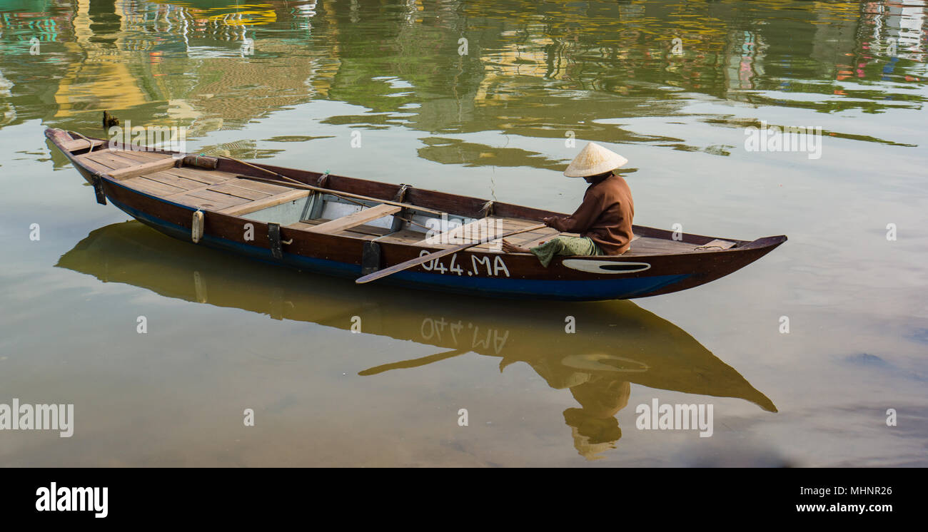 woman wearing iconic conical straw hat resting on her wooden boat with ...