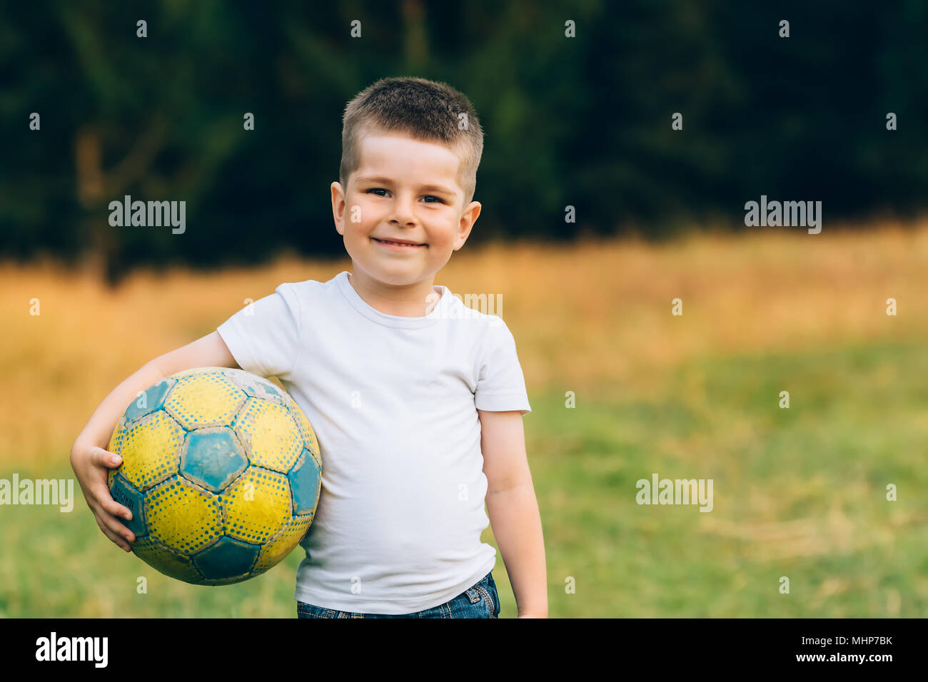 Child with a soccer ball under his arm at house garden with grass ...