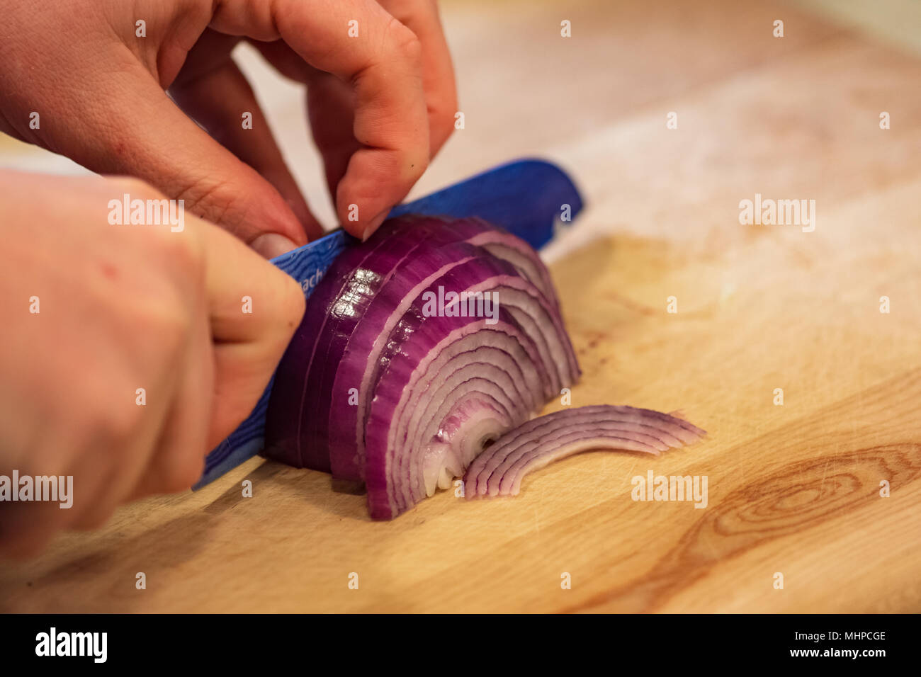 Hands cutting red onion with blue knife on cutting board Stock Photo ...