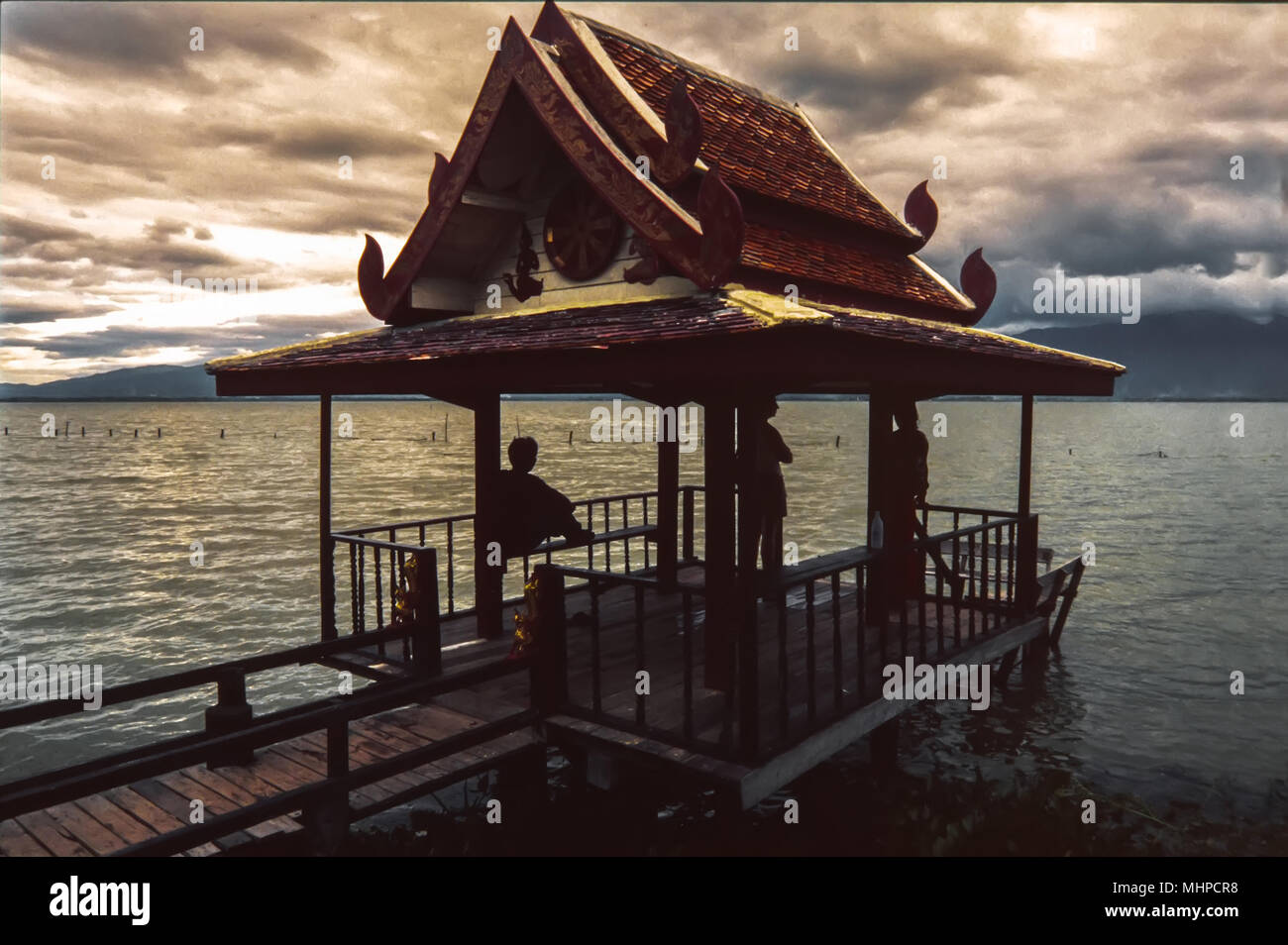 Silhouettes of people in traditional Thai house watching the ocean a ...