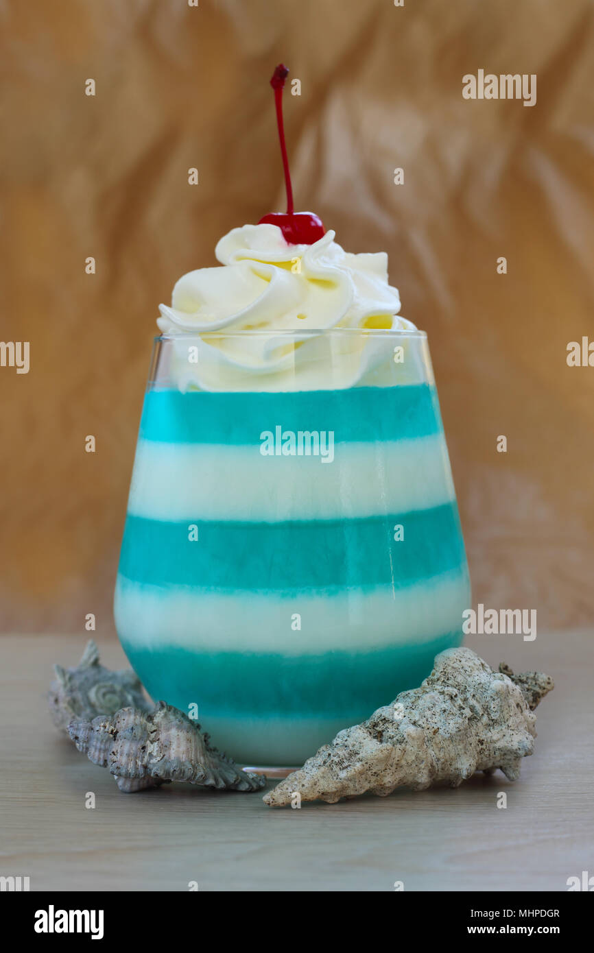Blue striped jello dessert in glass with whipped cream and red candied ...