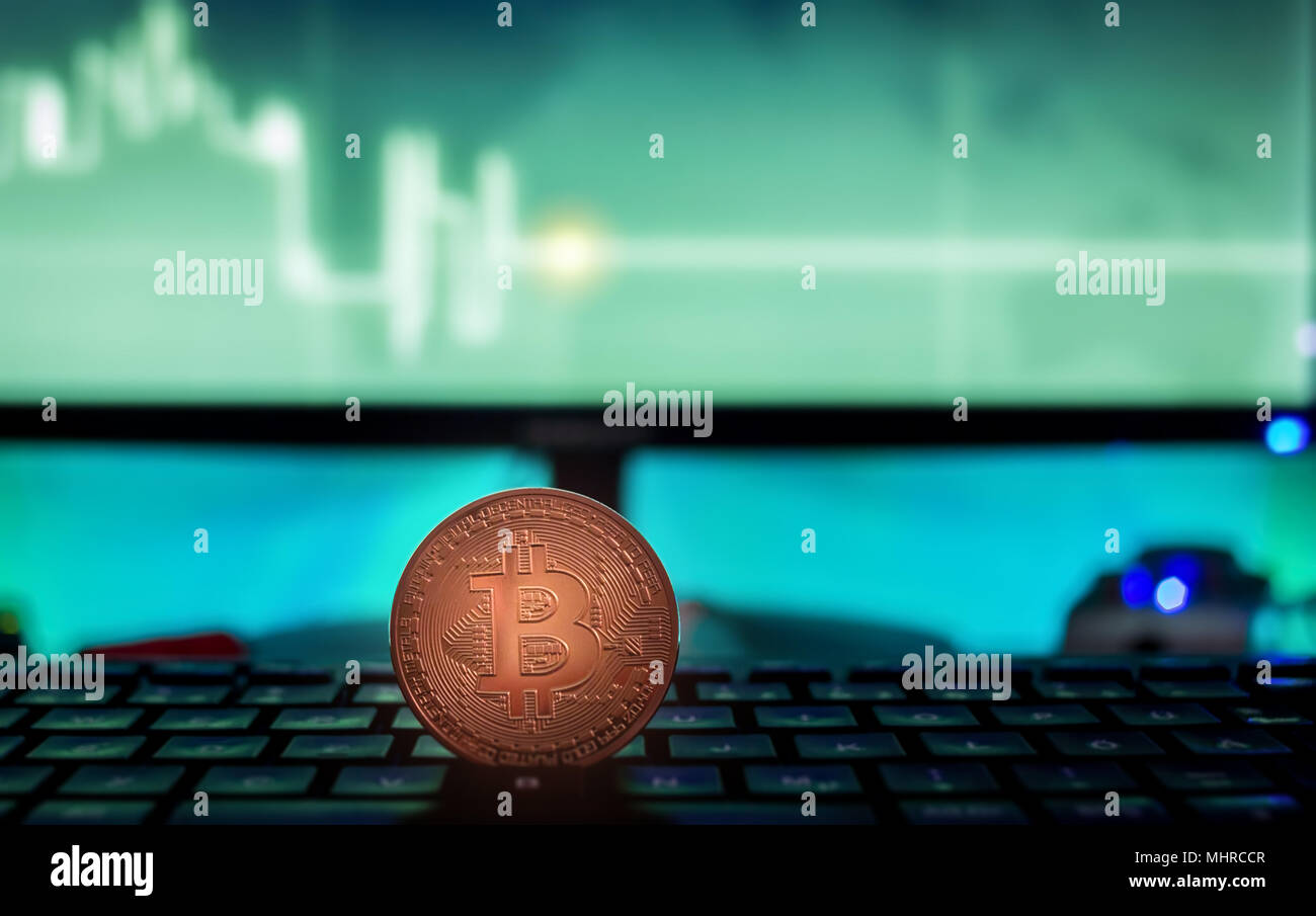 Physical Bitcoin placed on Laptop computer with charts on screen, dark ...