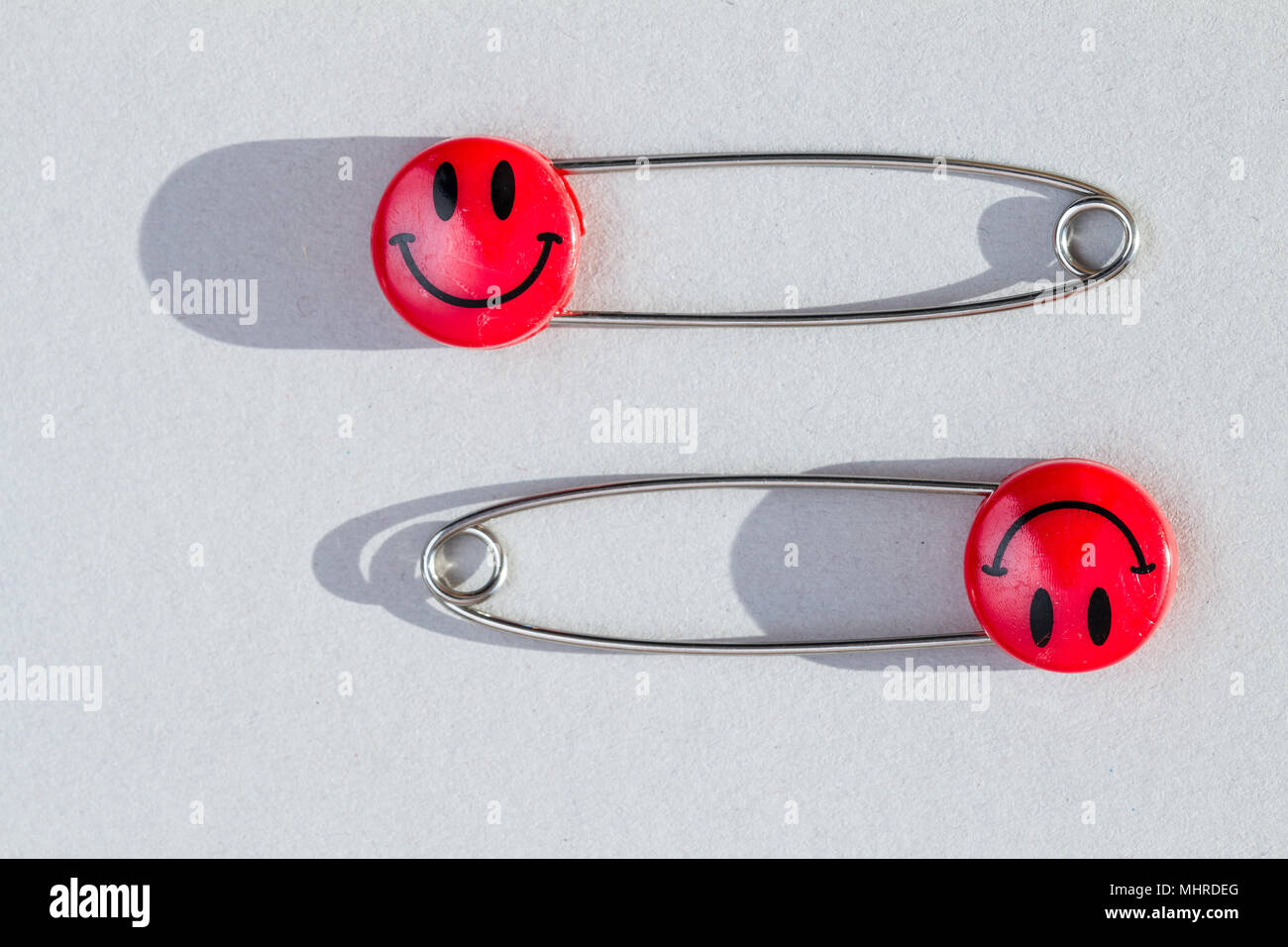 Plastic head metal safety pins pinned on grey paper. Red smile emoticon ...