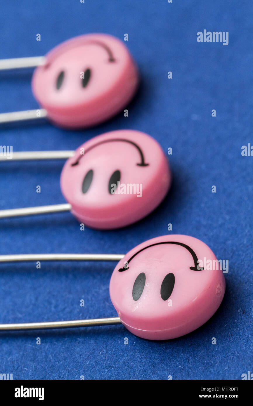 Plastic head metal safety pins pinned in paper. Pink smile emoticon ...