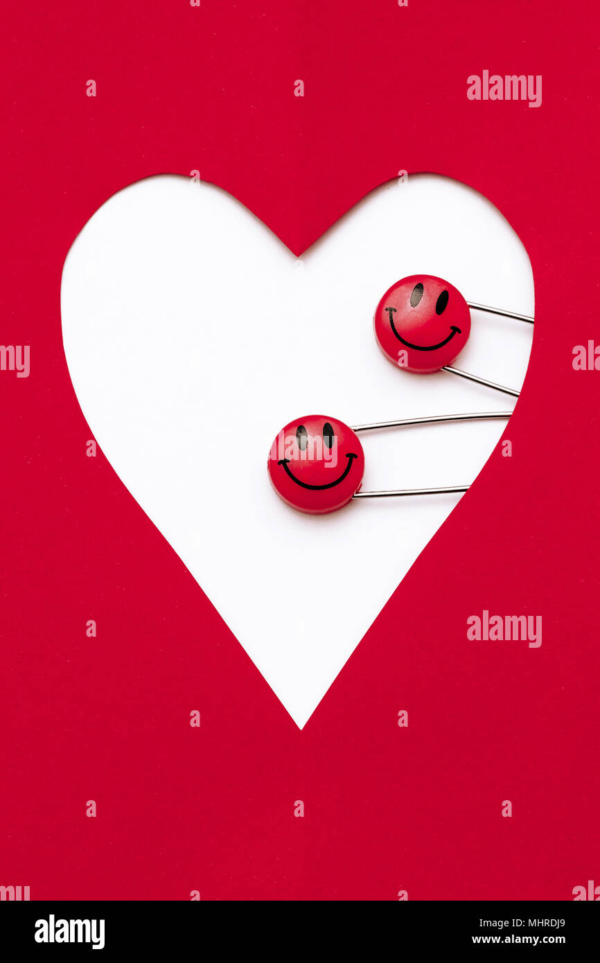 Plastic head metal safety pins pinned in heart shaped paper. Red smile ...