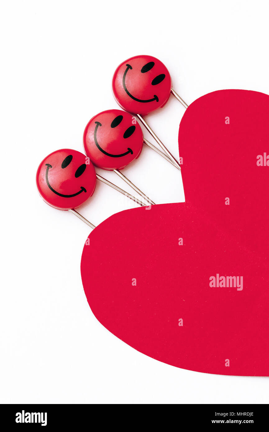 Plastic head metal safety pins pinned in heart shaped paper. Red smile ...