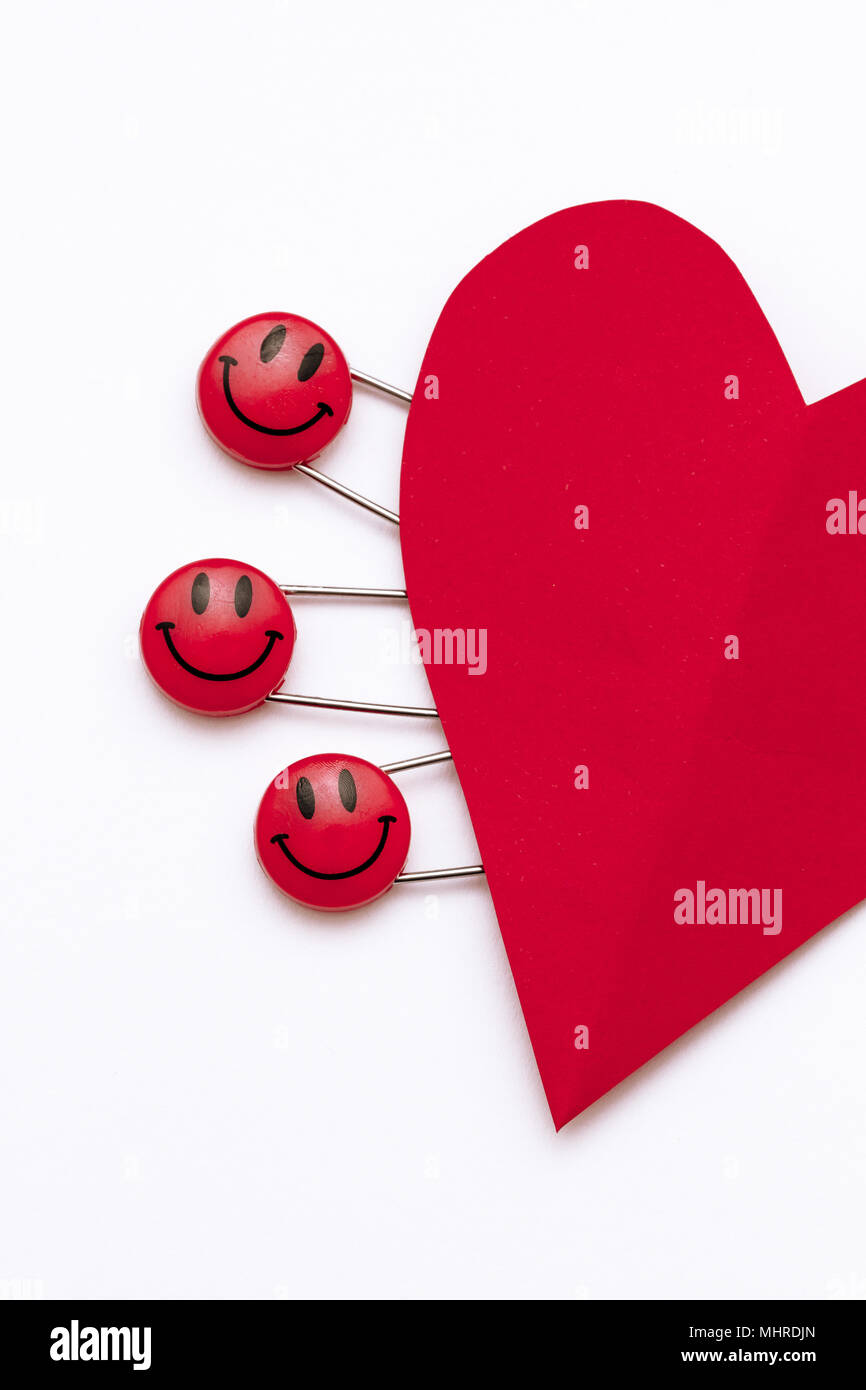 Plastic head metal safety pins pinned in heart shaped paper. Red smile ...