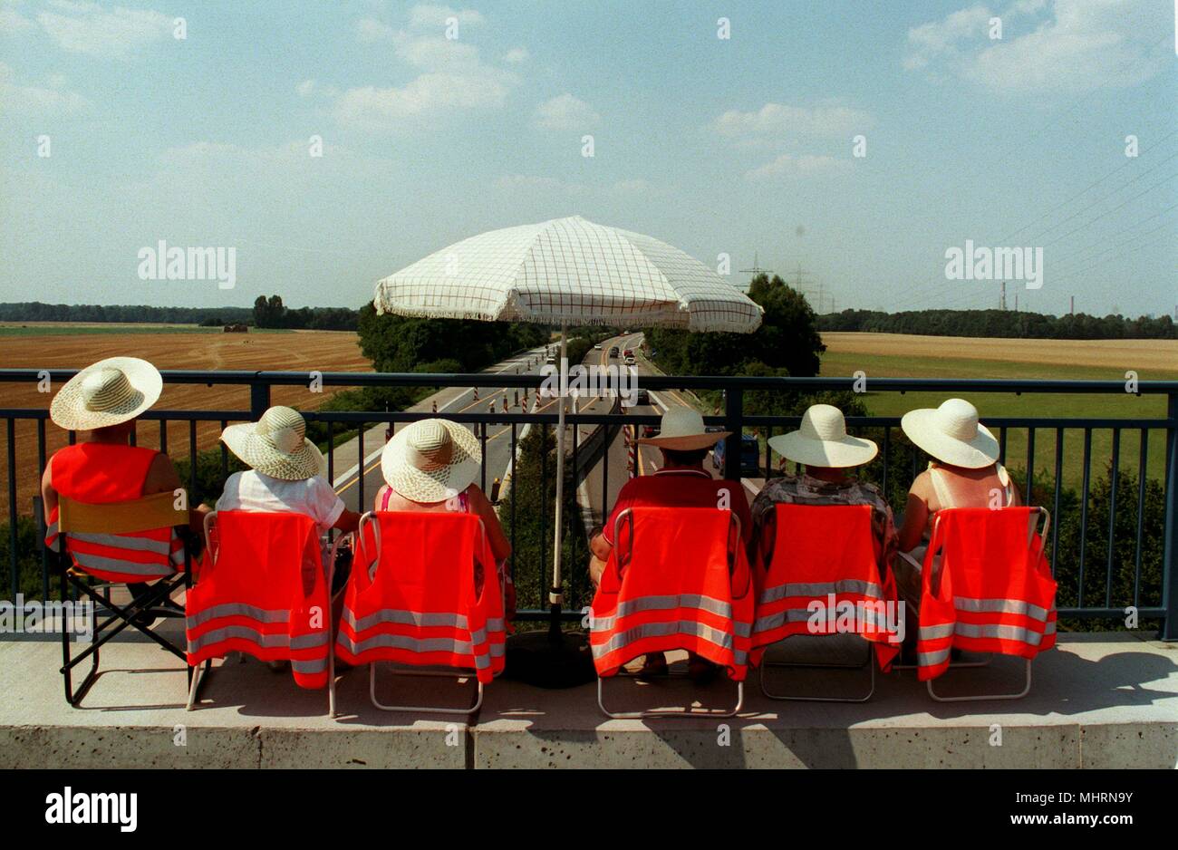 protected by wide-brimmed sun hats and a parasol against the heat of ...