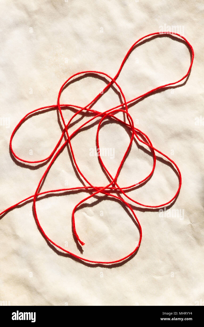 Red thread of thick red yarn fiber on grungy crumpled aged white paper ...