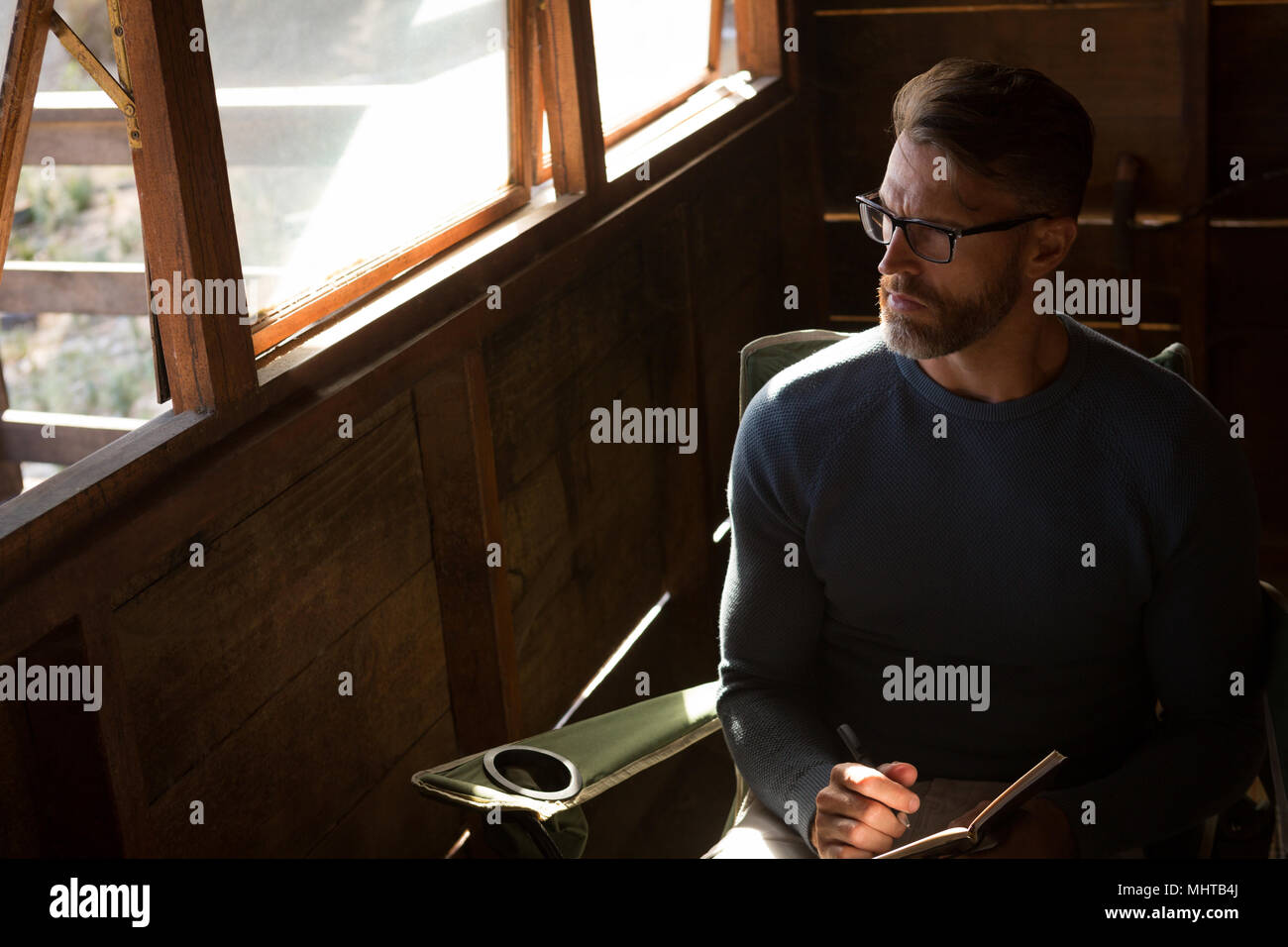 Thoughtful man sitting on chair and looking through window Stock Photo ...
