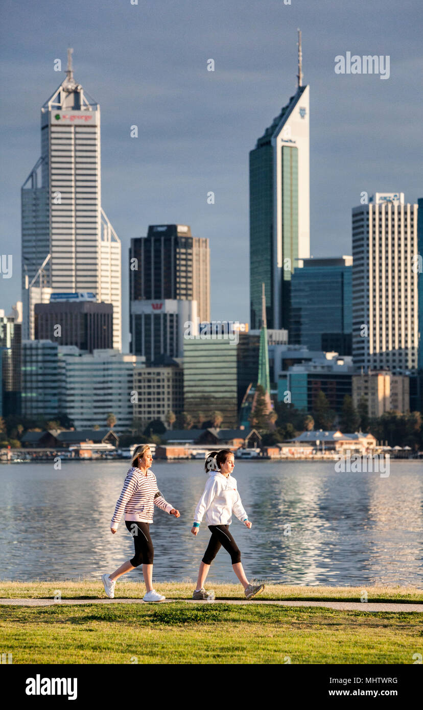 Two women walking beside the Swan River in South Perth with Perth city ...
