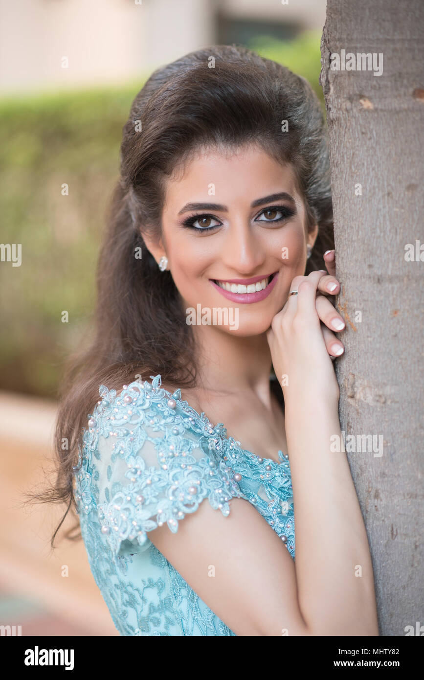 Beautiful woman leaning against a tree smiling Stock Photo - Alamy