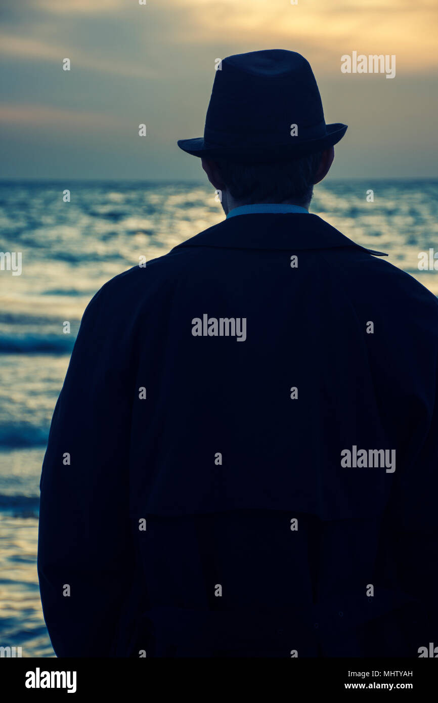 Rear view of a man wearing a coat and hat on the beach at sunset Stock ...