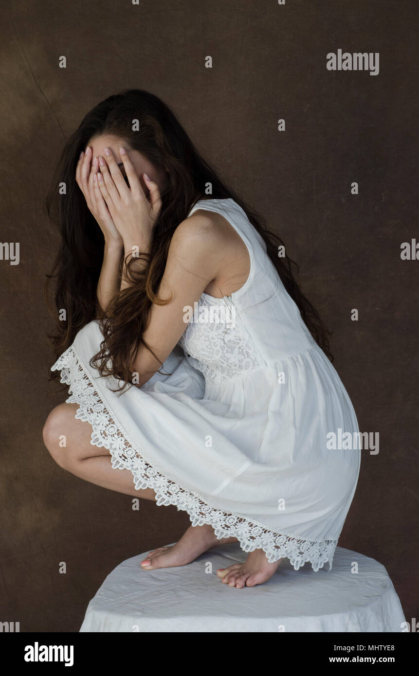 Scared woman crouching over a table hiding face with hands Stock Photo ...