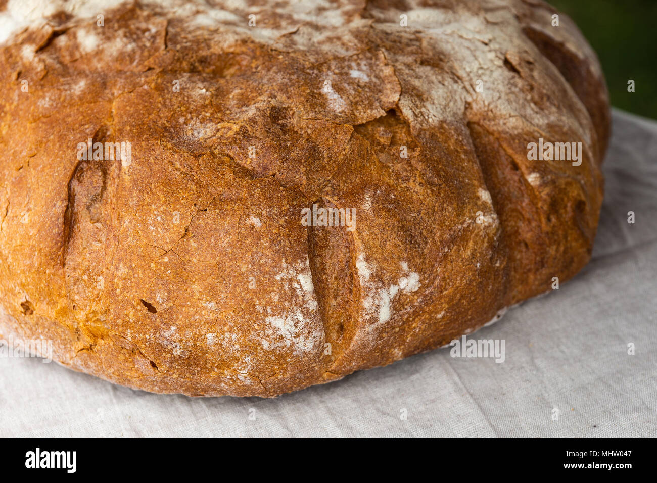 Loaf of fresh bread with a golden brown crust. White linen cloth under ...