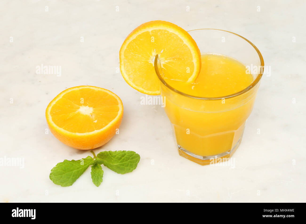 Fresh orange juice in a glass with a half orange on a marble worktop ...