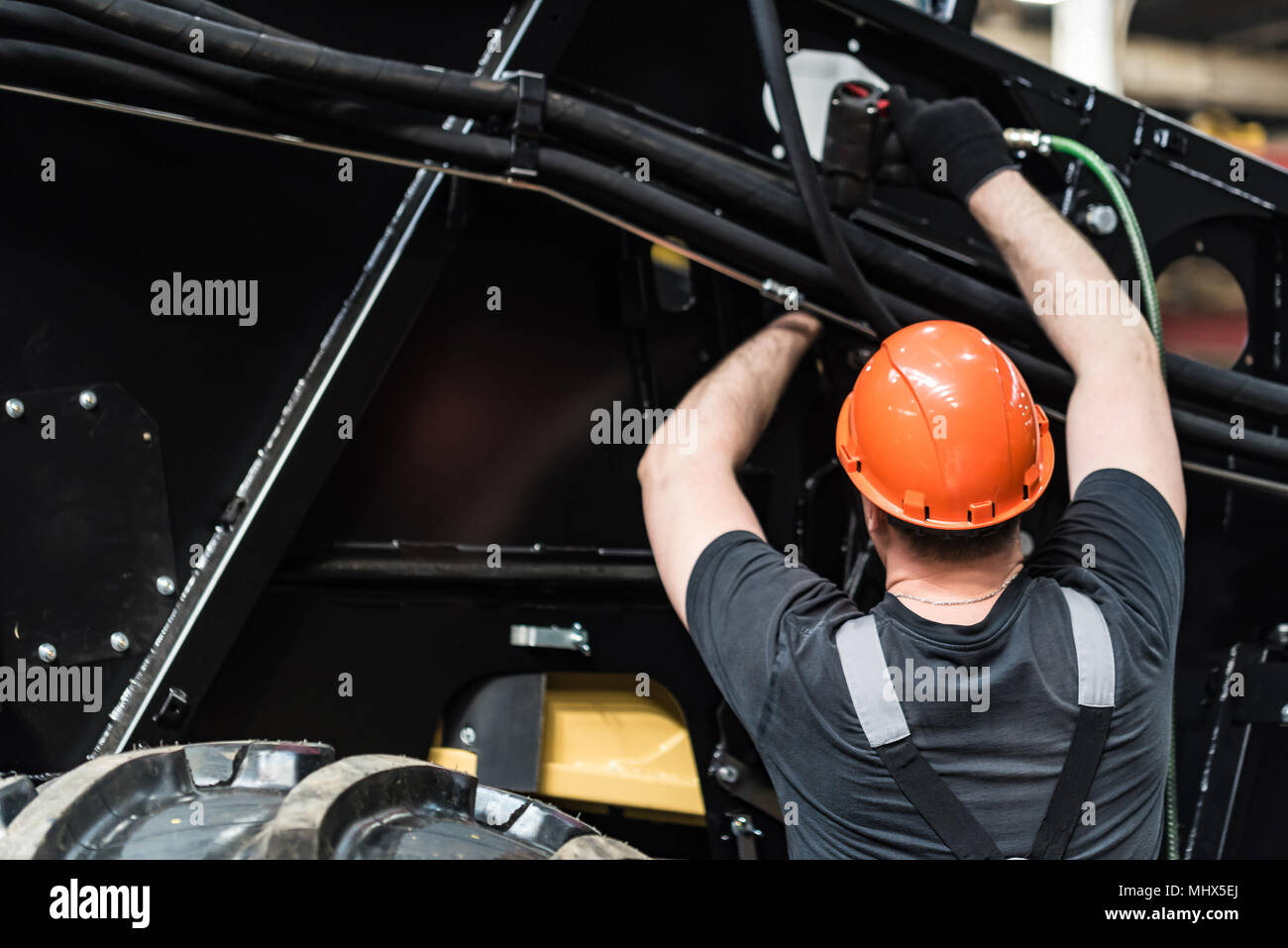 Worker assembles tractor or combine harvester at large machinery plant ...