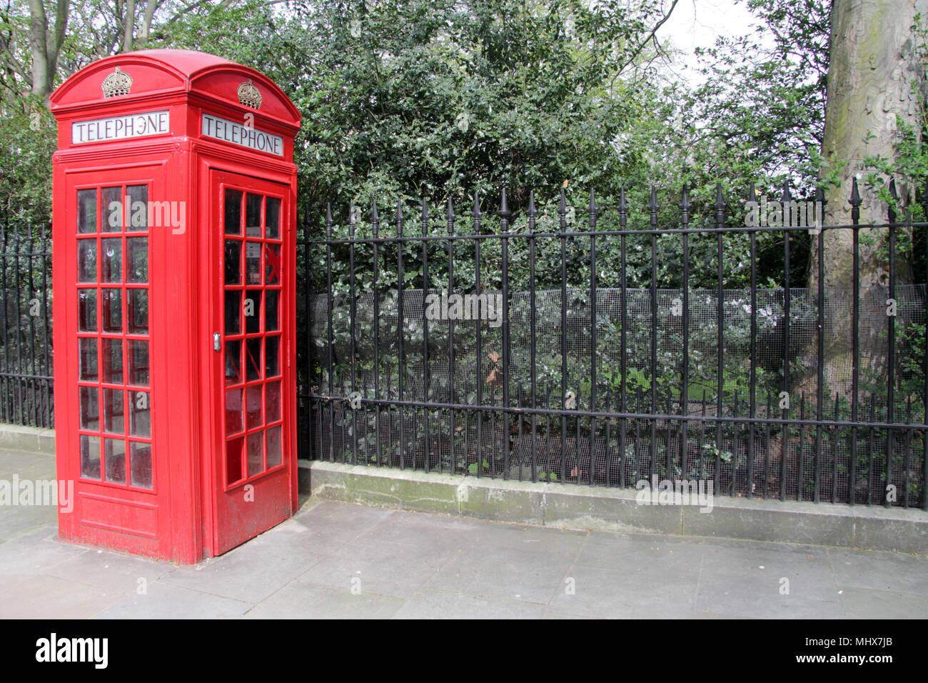Red London Telephone Box, on pavement by fence outside a park Stock ...