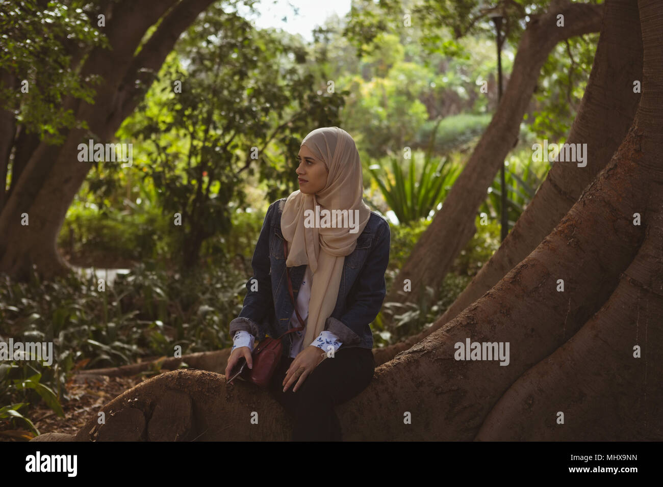 Hijab woman sitting on tree root in garden Stock Photo - Alamy
