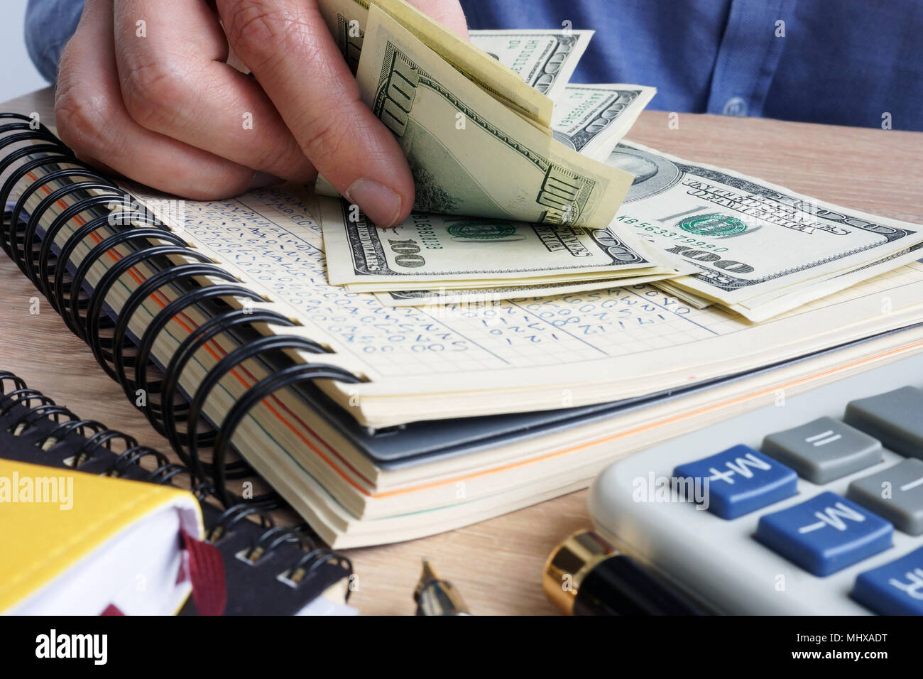 Man counting dollar bills. Desk with calculator, ledger and dollars ...