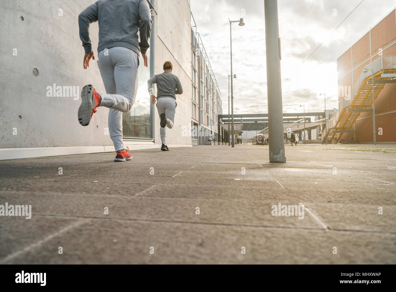 Young adult male twin runners, running along city sidewalk, rear view ...