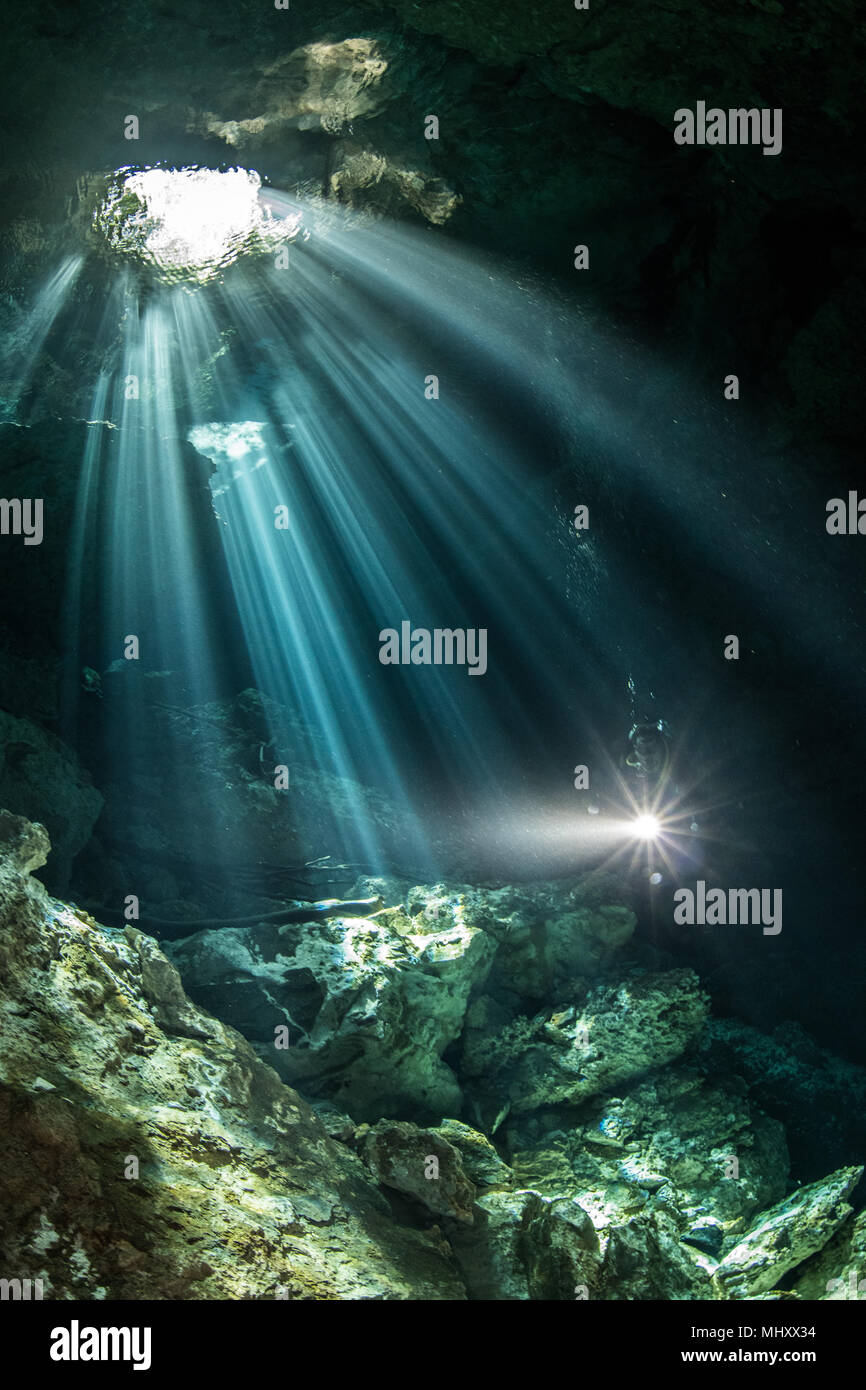 Male diver diving in underground river (cenote) with sun rays and rock ...