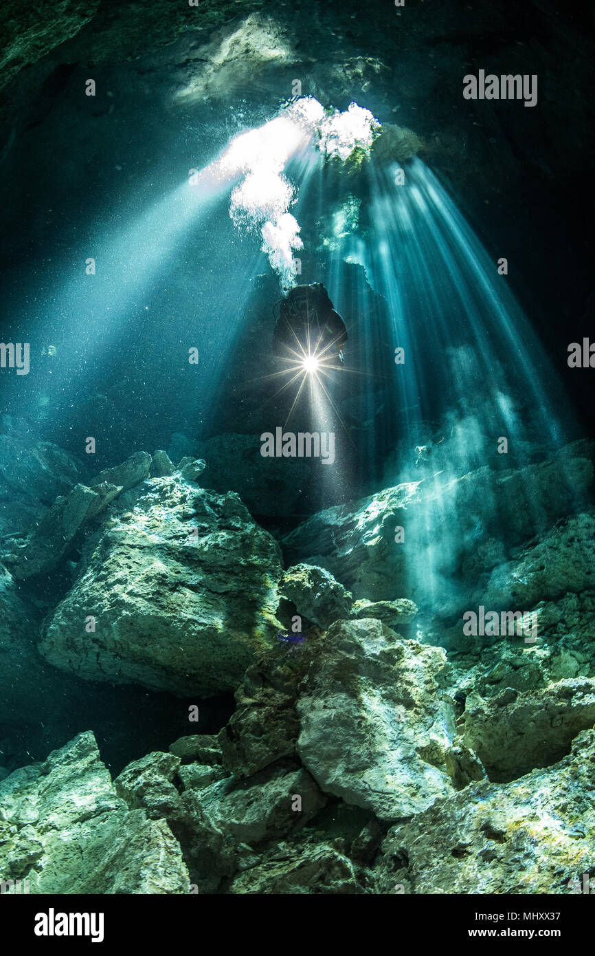Male diver diving in underground river (cenote) with sun rays and rock ...