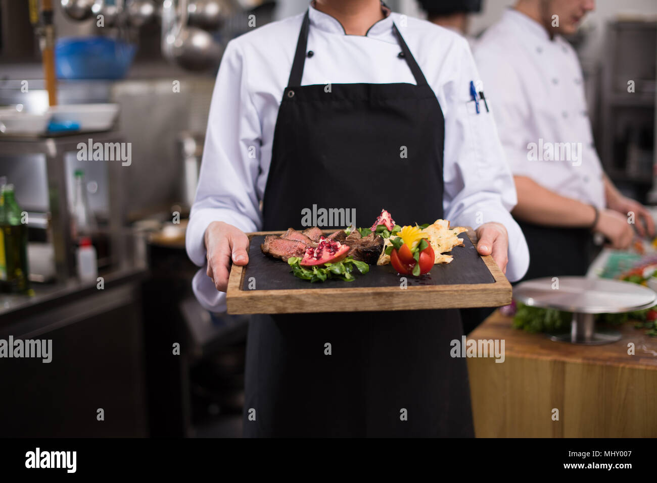female Chef in hotel or restaurant kitchen holding grilled beef steak ...