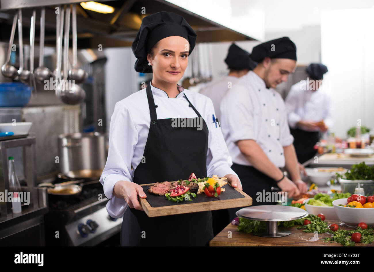 female Chef in hotel or restaurant kitchen holding grilled beef steak ...