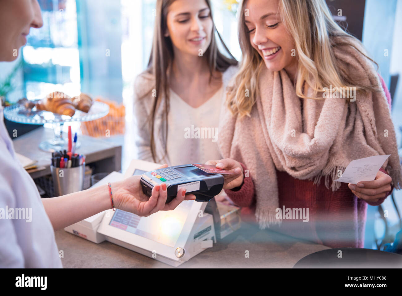 Female friends standing at counter in cafe, paying using credit card ...