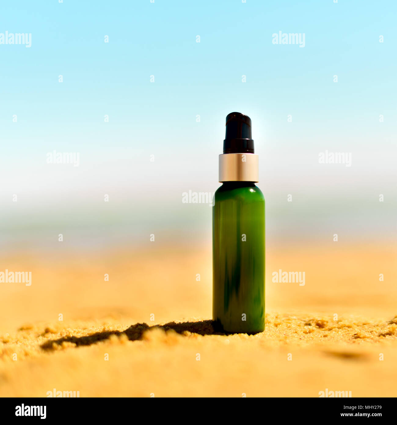 Bottle of sunscreen in sand against sea background with copyspace ...