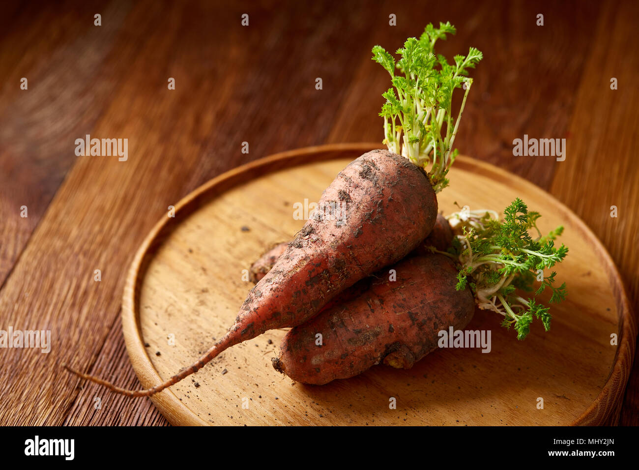 Bundle of carrots with soil on wooden plate over rustic wooden ...