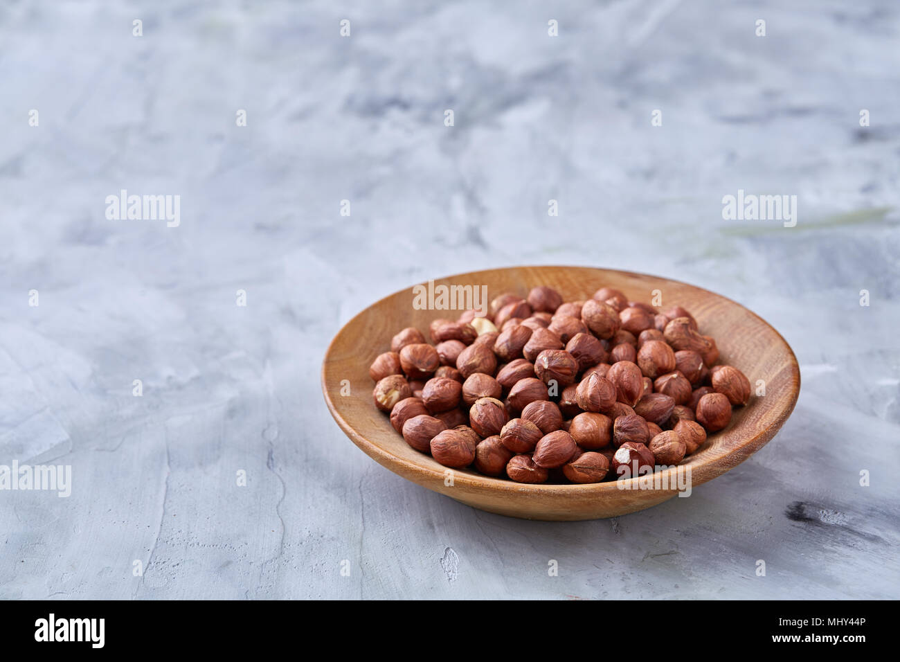 Hazelnuts in clay ceramic bowl on white textured background with copy ...