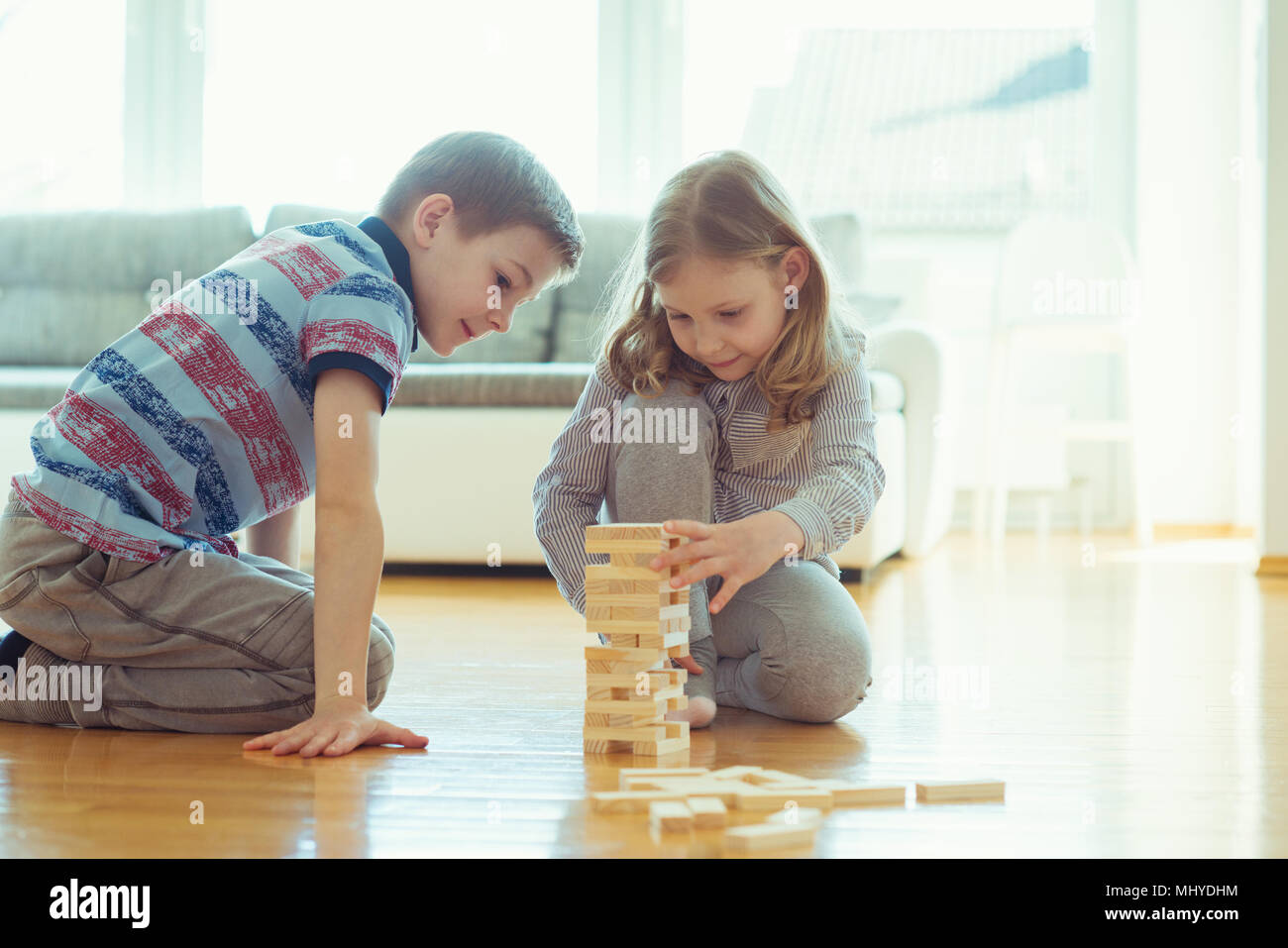 Two happy siblings playing a game with wooden blocks at home joyfully ...