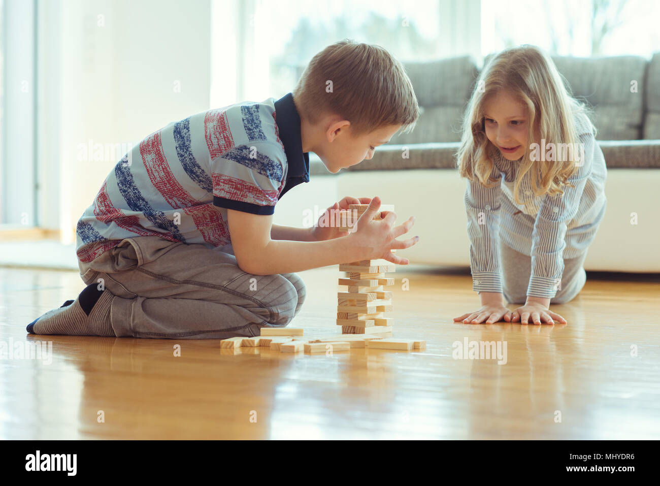 Two happy siblings playing a game with wooden blocks at home joyfully ...
