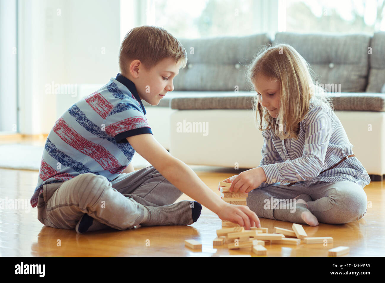 Two happy siblings playing a game with wooden blocks at home joyfully ...