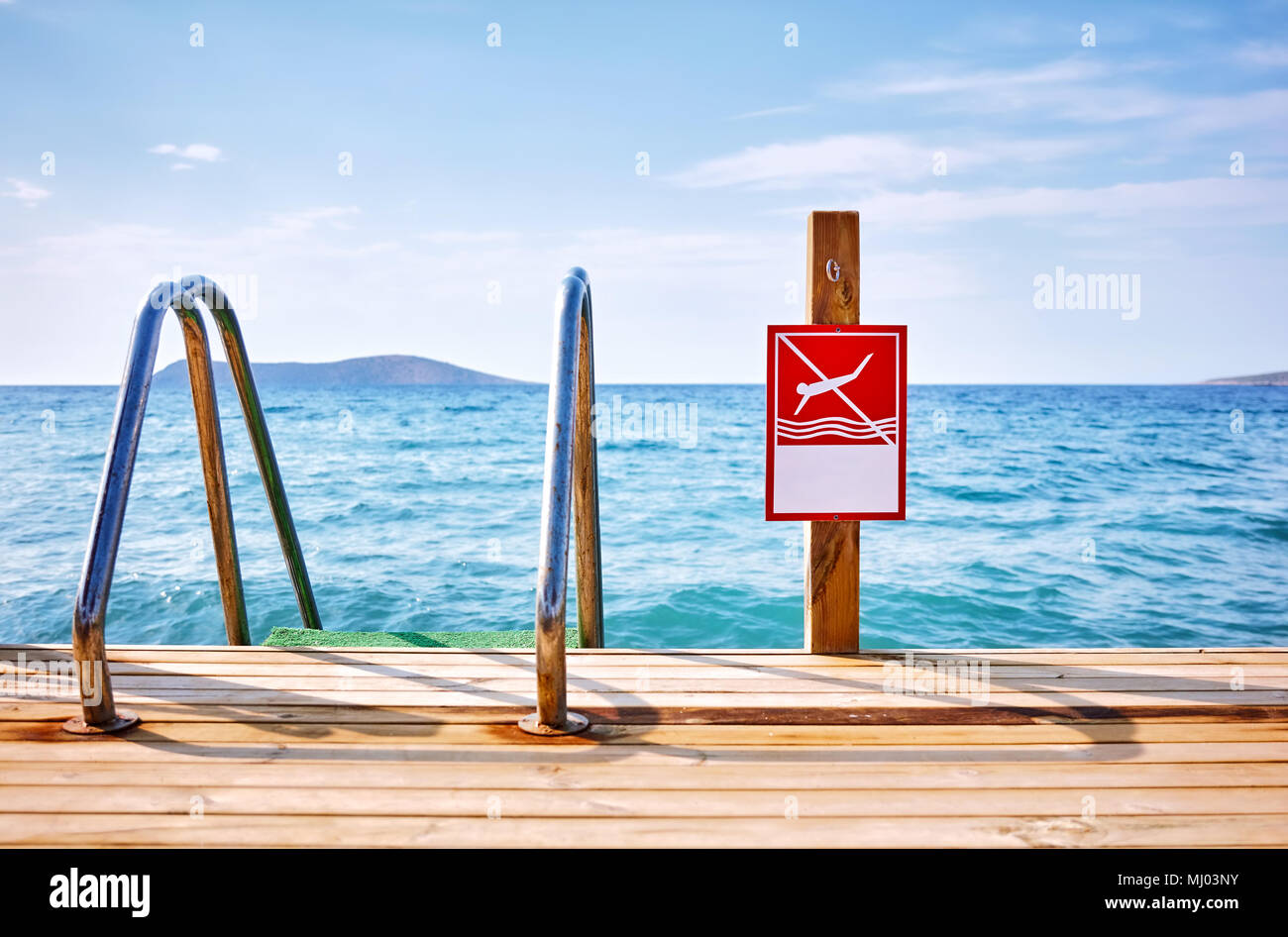 Red no diving sign with copy space on a wooden pier next to a ladder ...