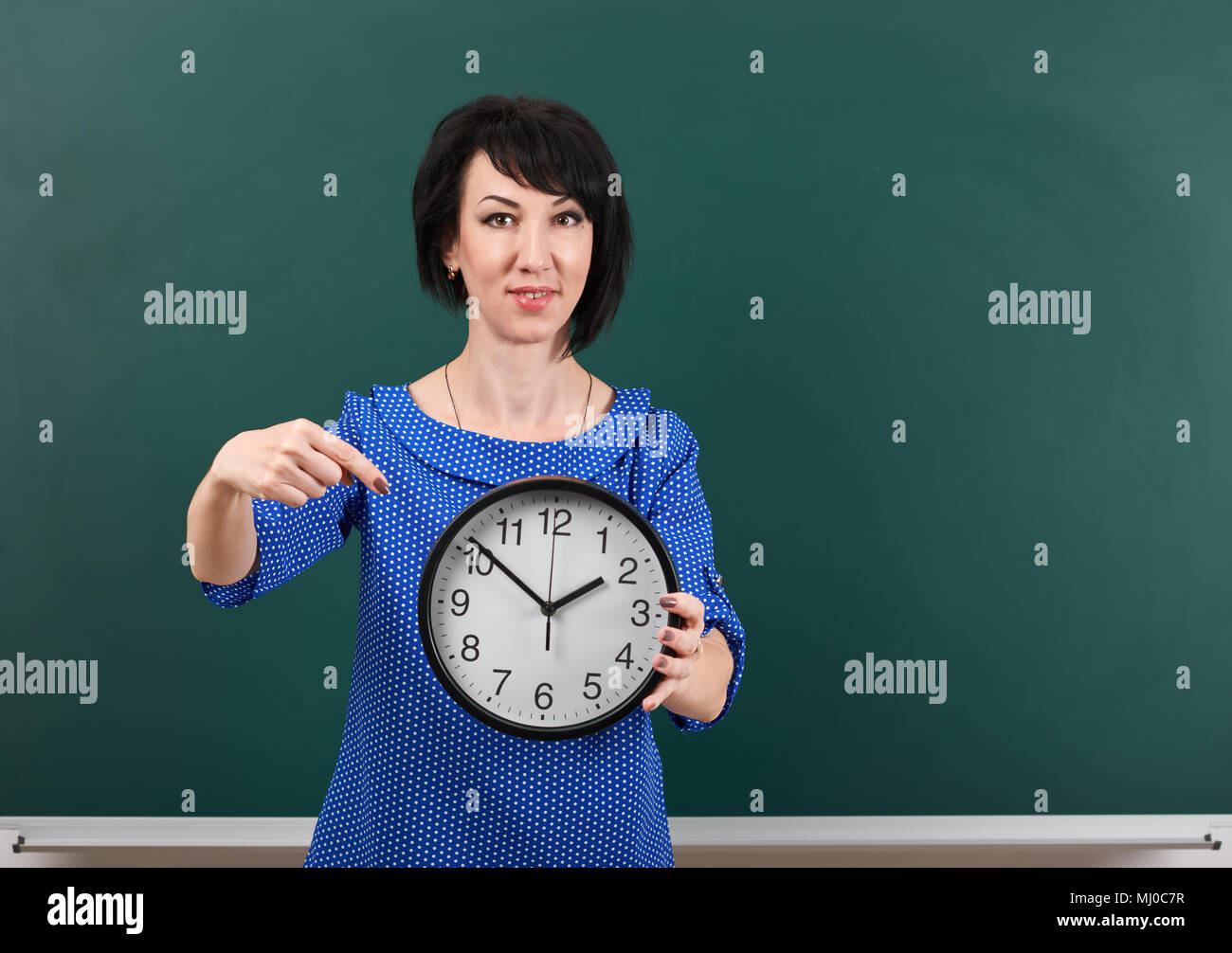 woman pointing finger at the watch, posing by chalk board, time and ...