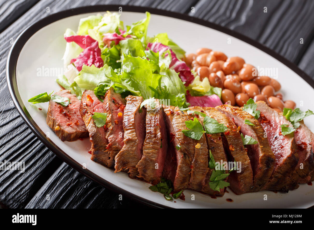 Grilled sliced carne asada beef steak with lettuce and beans close-up ...