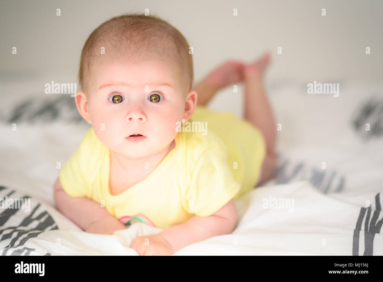 Curious 4 months old Baby girl on a bed looking into camera with her ...