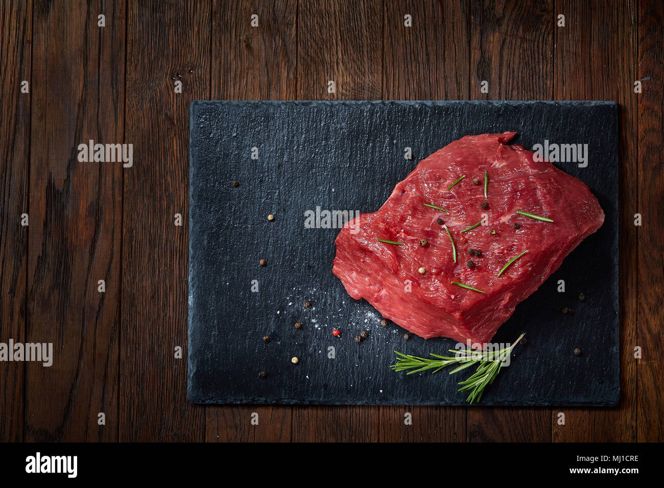Raw meat beef steaks on black slate board with spices and rosemary over ...