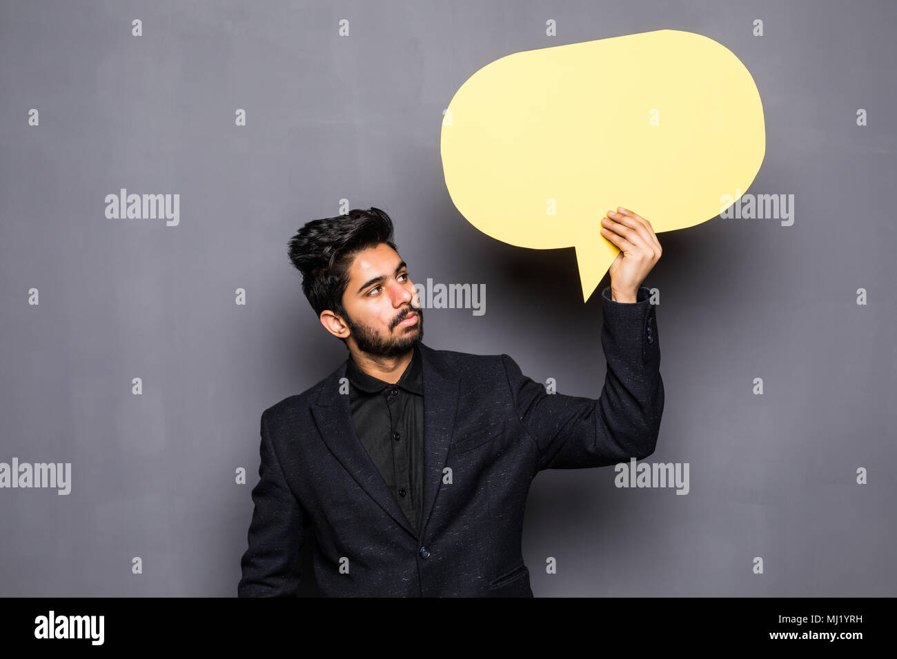 Young indian business man holding a bubble for text, isolated on grey ...