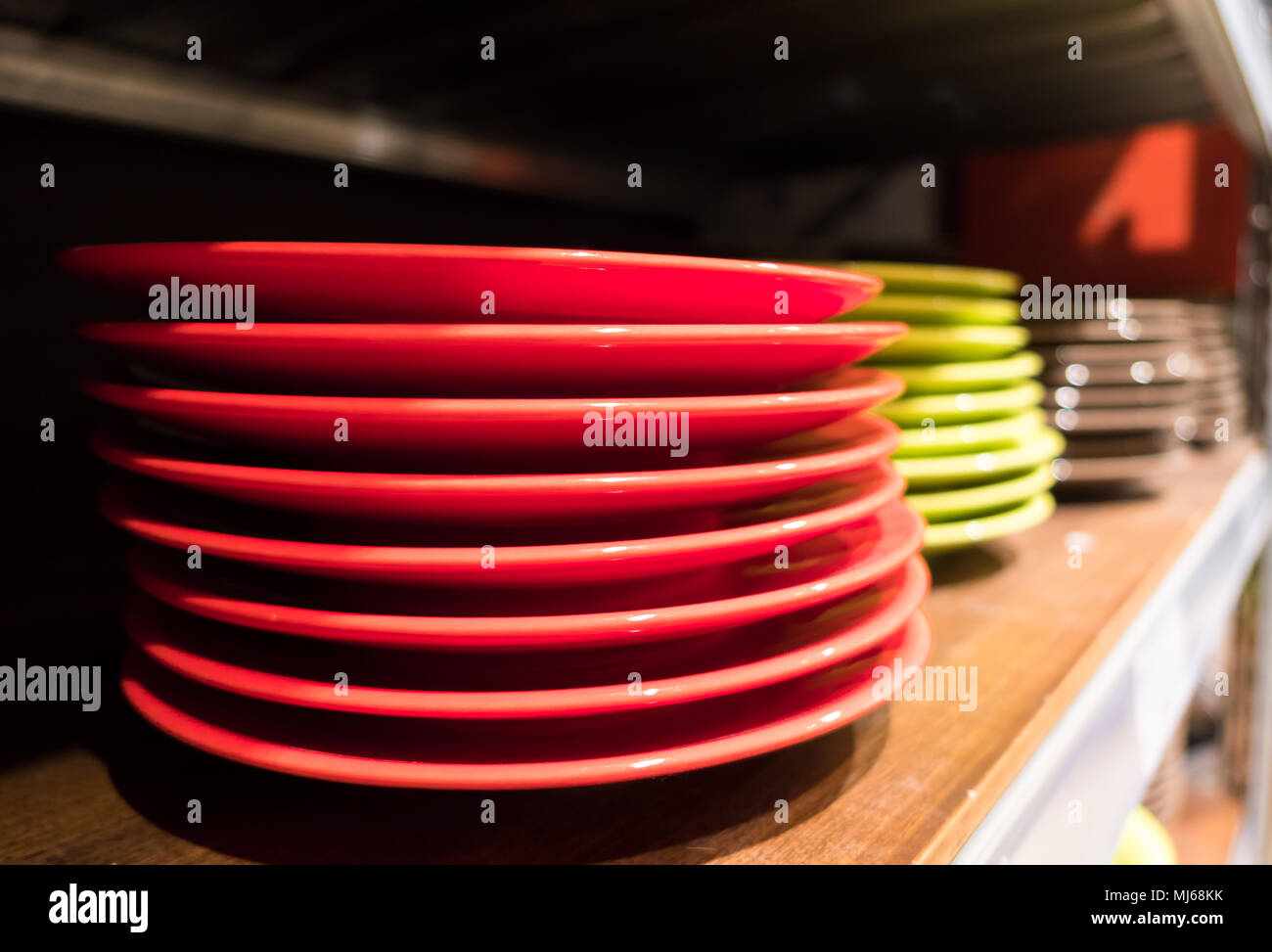 Colored dishes (red, green and white) on a wooden bookshelf, on a ...